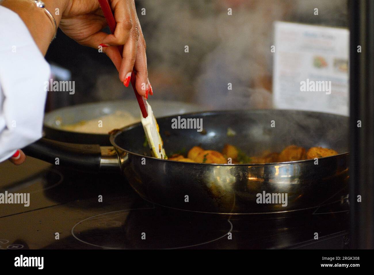 Female cook holds a spatula while stirring food in a pan, steam coming off of it indicating it ...
