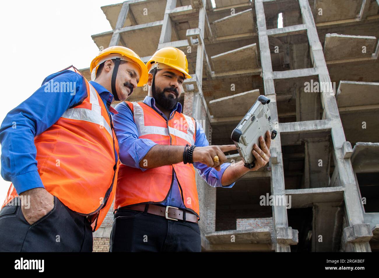 Two Indian male civil engineers or architect wearing helmet and vest holding digital tablet ...