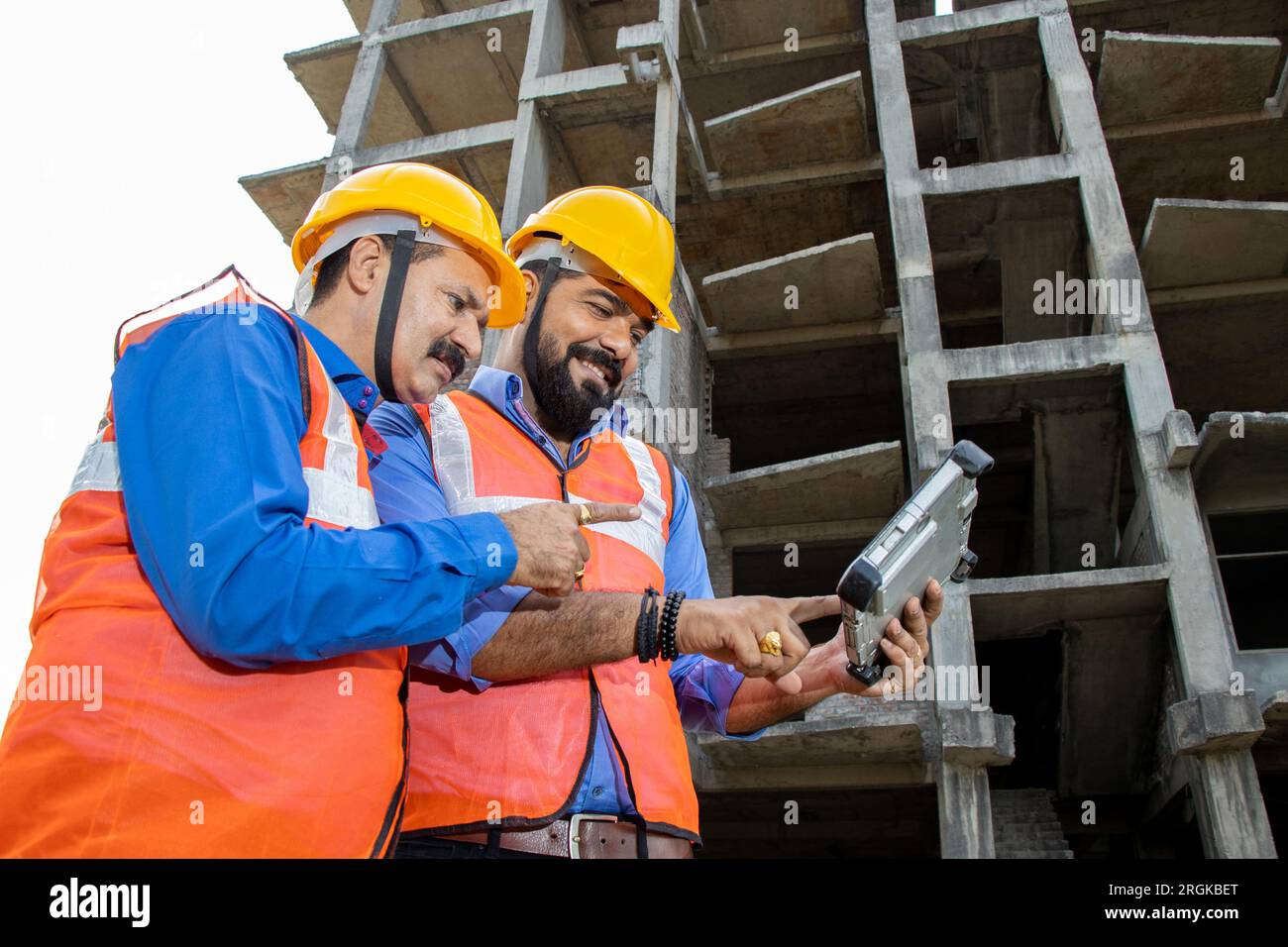 Two Indian male civil engineers or architect wearing helmet and vest holding digital tablet ...