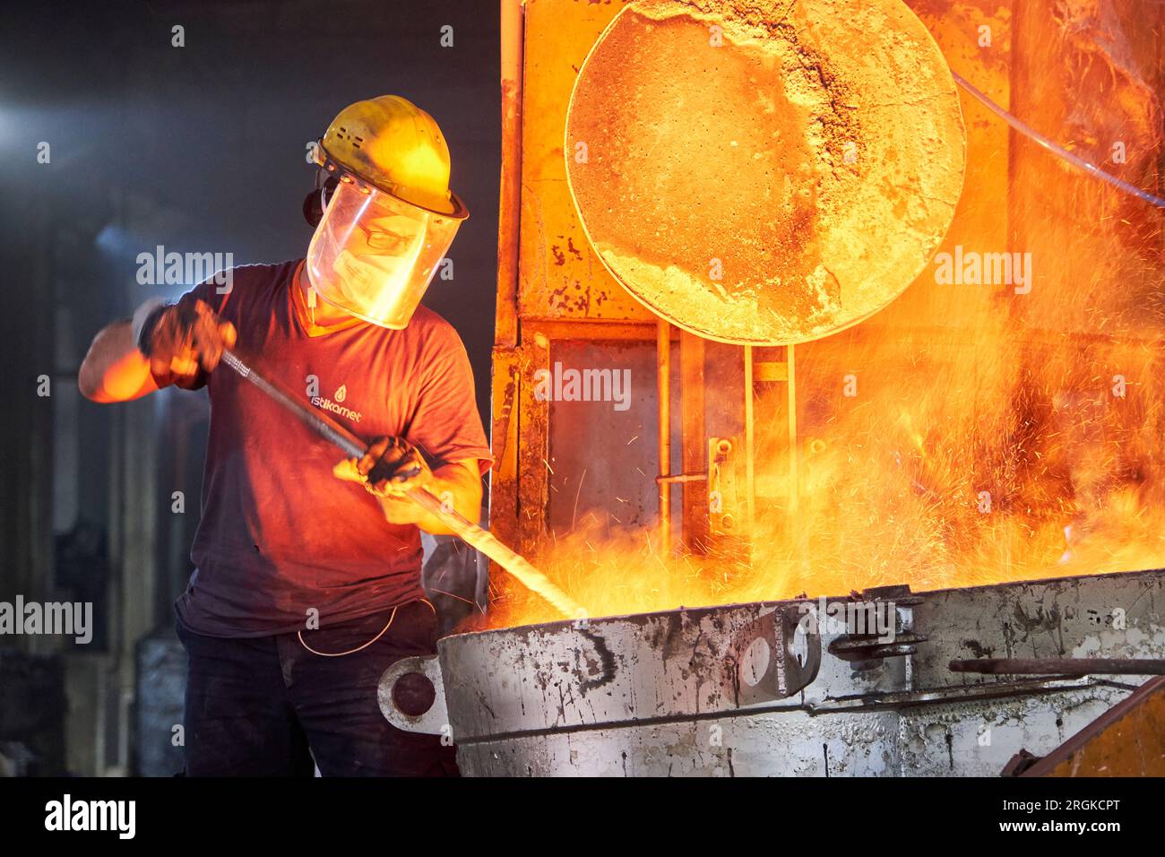 factory worker with helmet and safety gear steering a big pot of melted ...