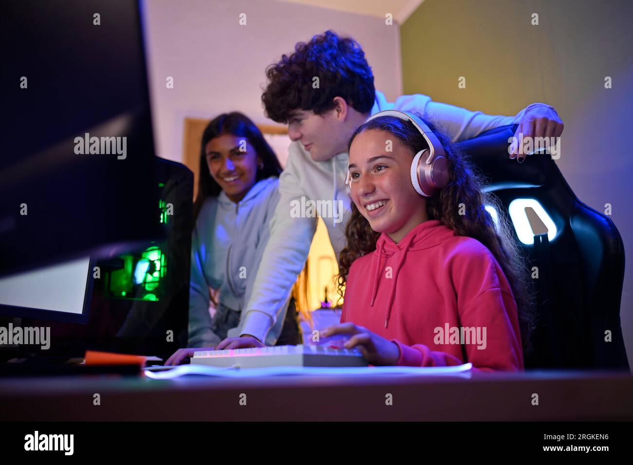 Smiling young teenage girl in headphones looking at screen of monitor ...