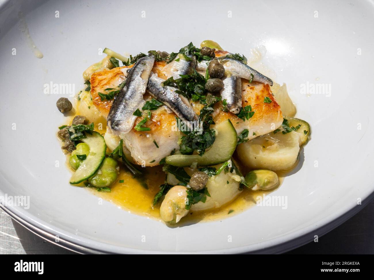 prepared dish of pan fried cod with whitebait capers courgette and ...