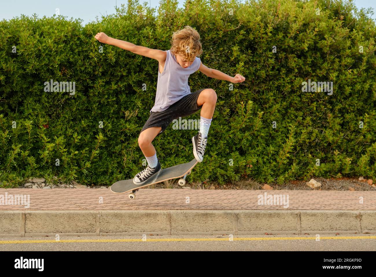Active preteen skater jumping with skateboard above asphalt road and ...