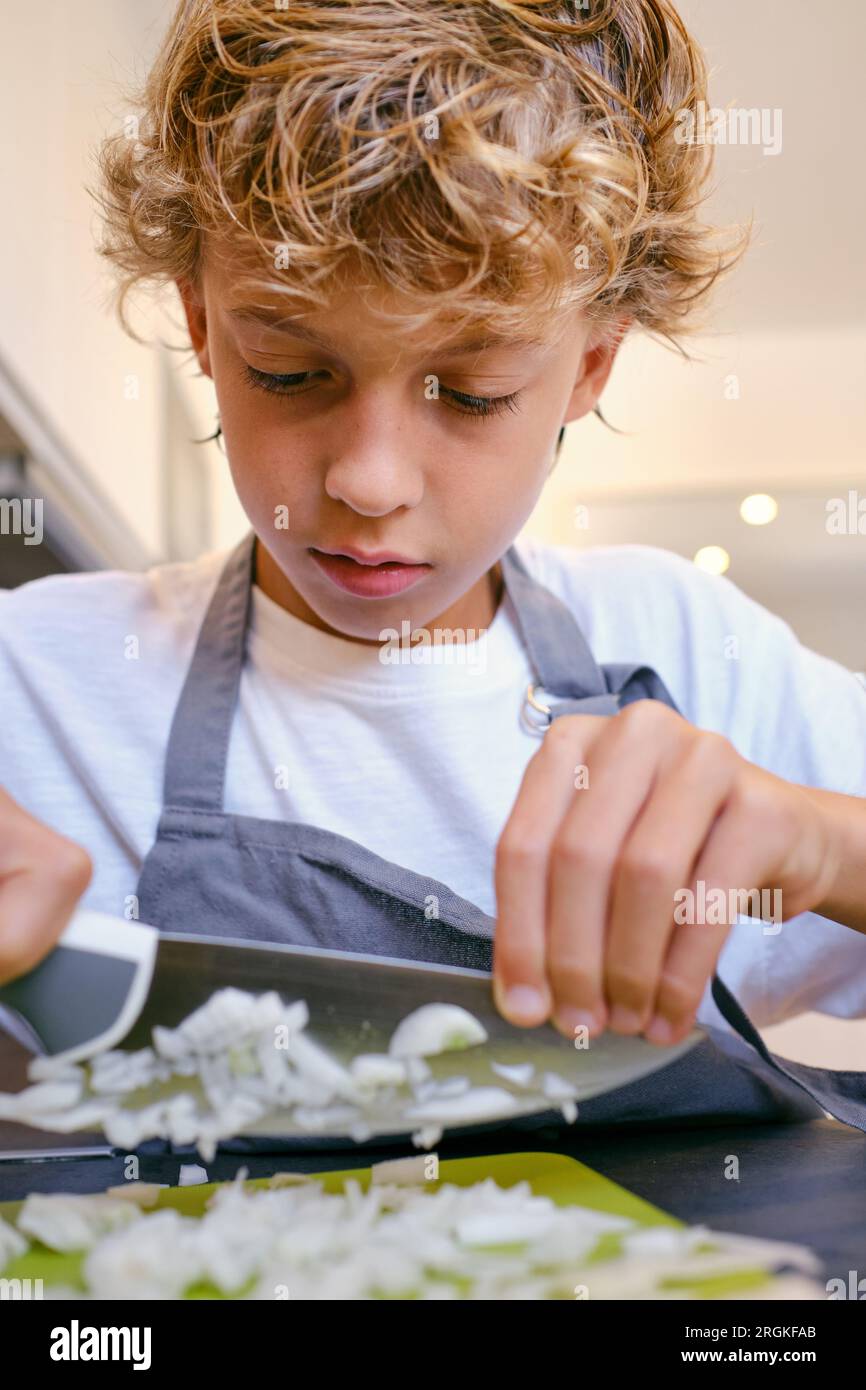 Crop focused child with wavy hair and knife chopping fresh onion while ...