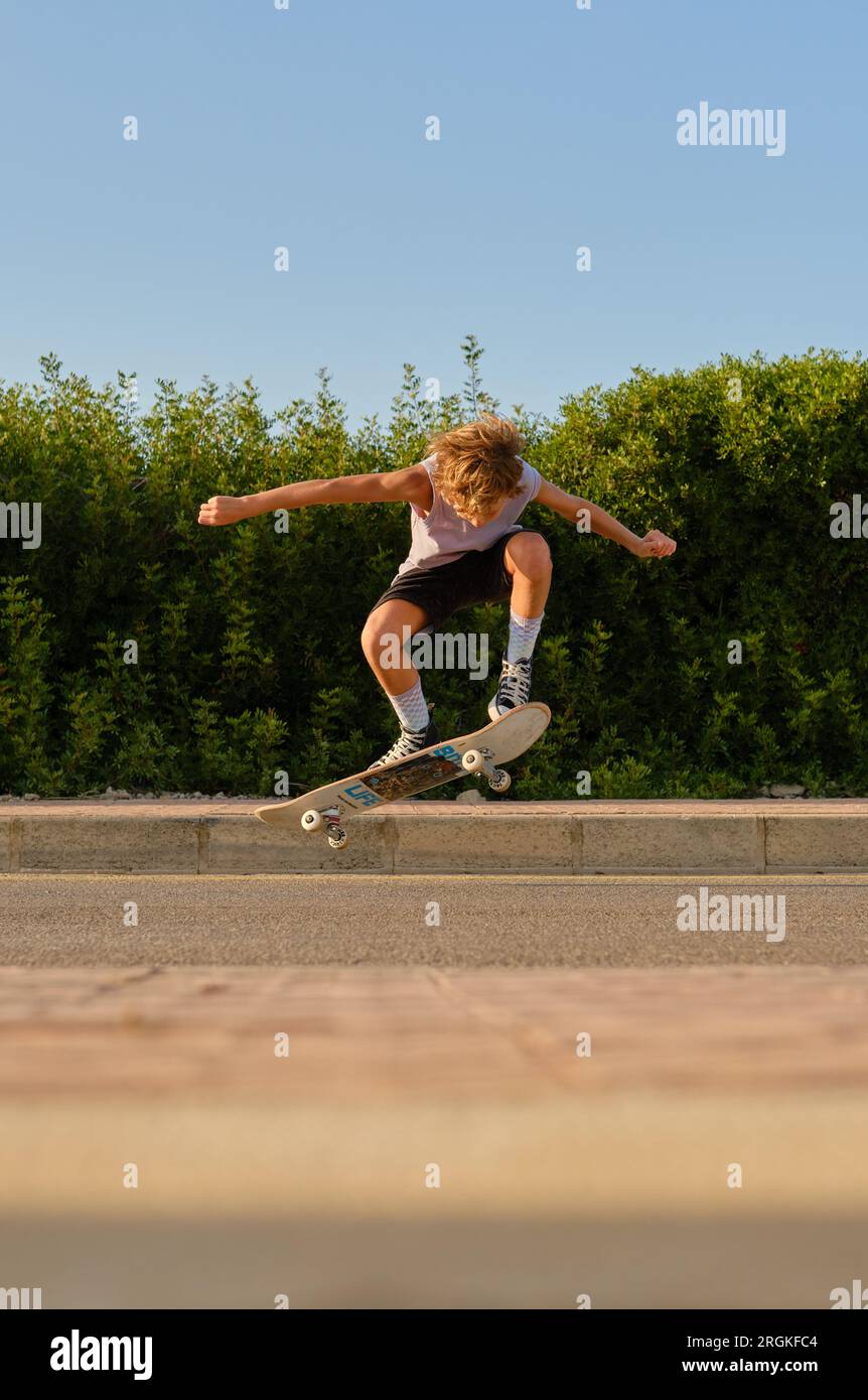 Ground level of cool preteen boy jumping with skateboard over road and ...