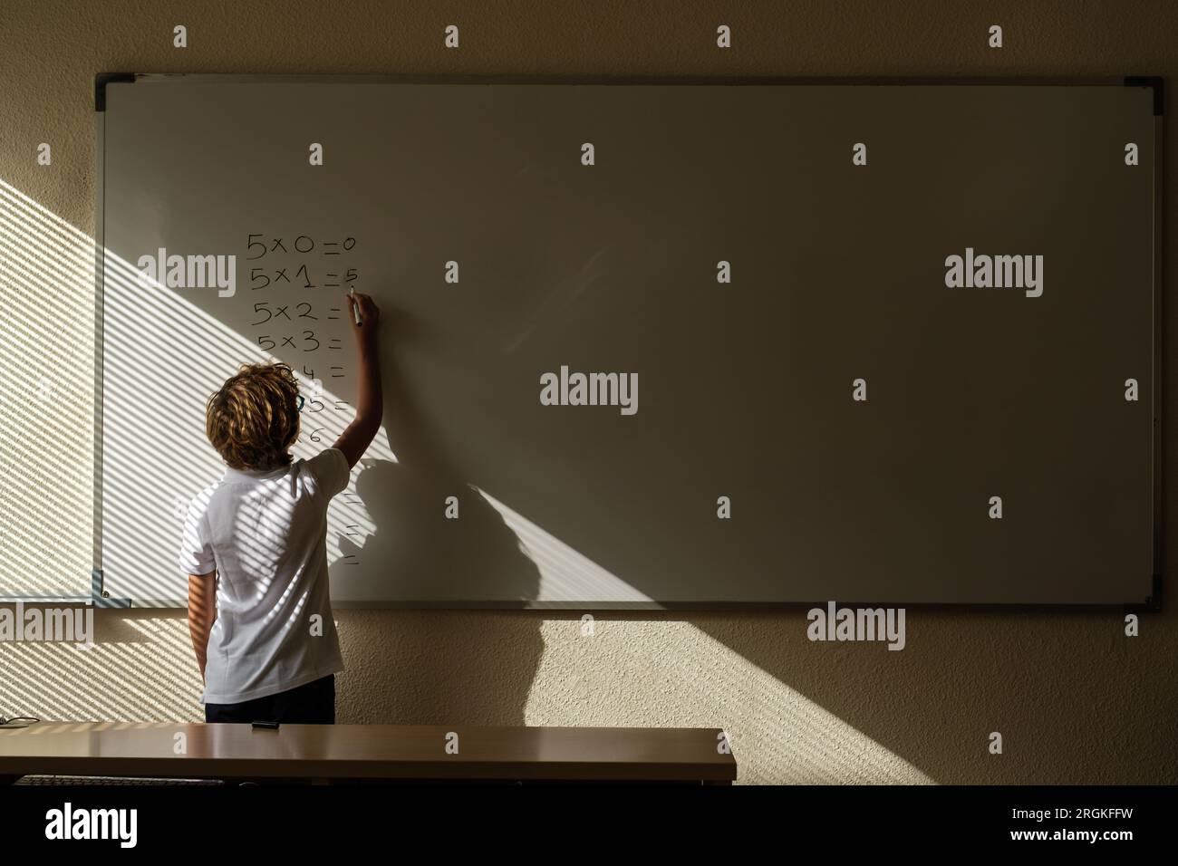 Back view of anonymous schoolboy writing multiplication table on ...