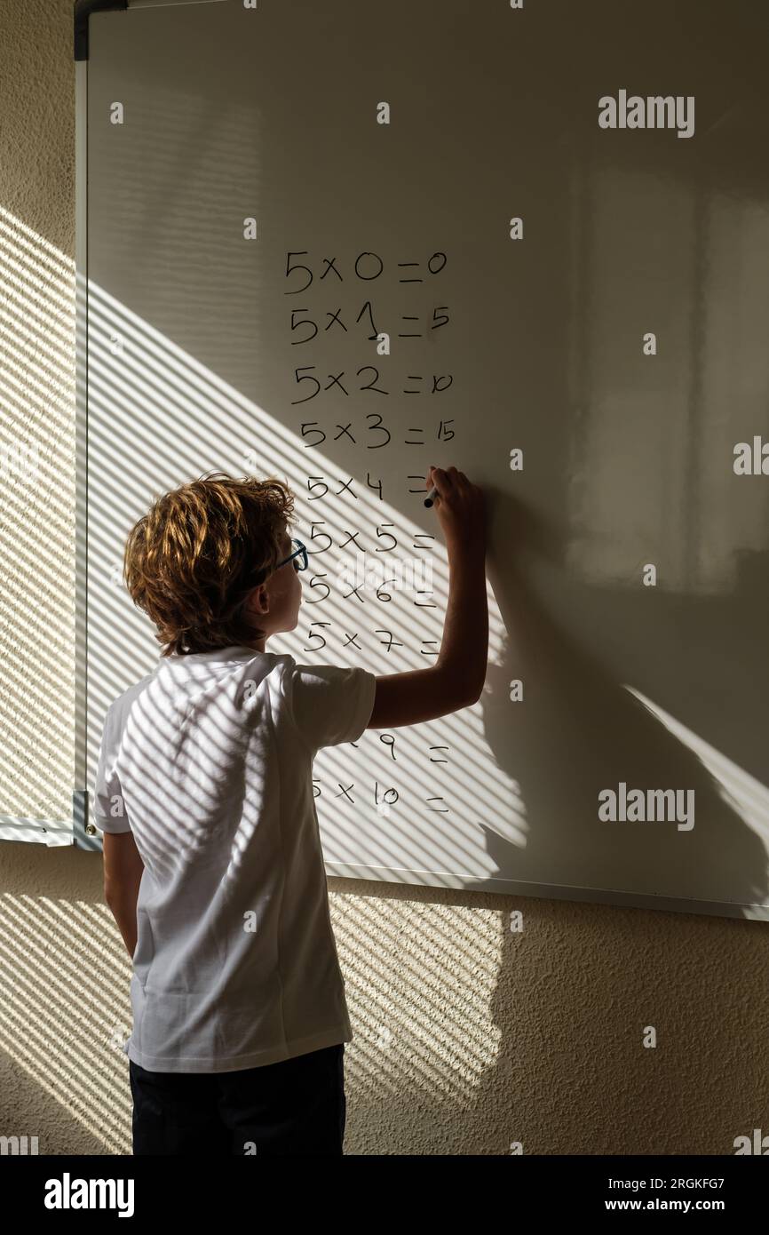 Back view of intelligent schoolboy standing writing multiplication ...