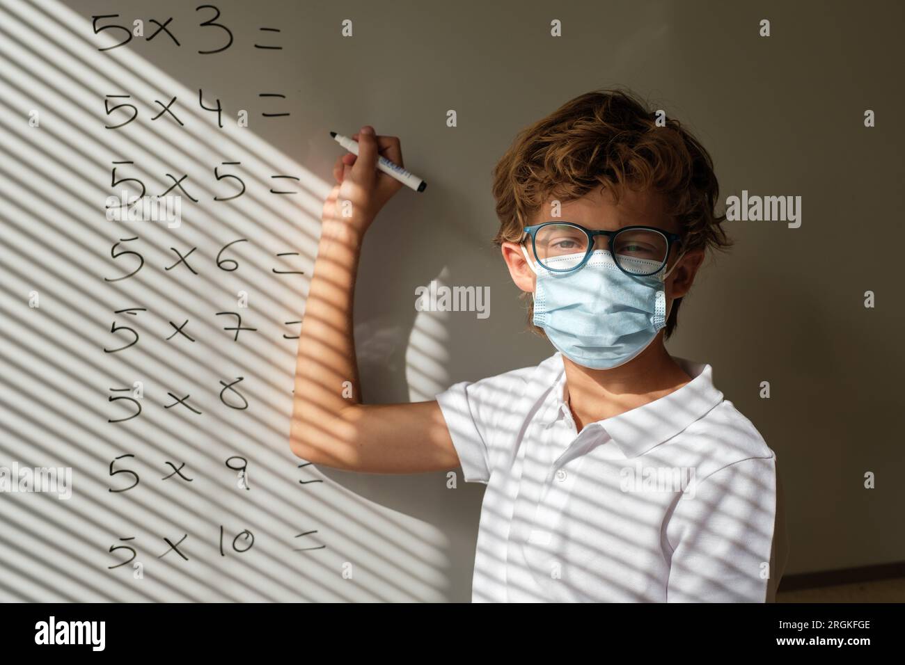 Schoolchild in glasses and protective mask solving mathematical ...
