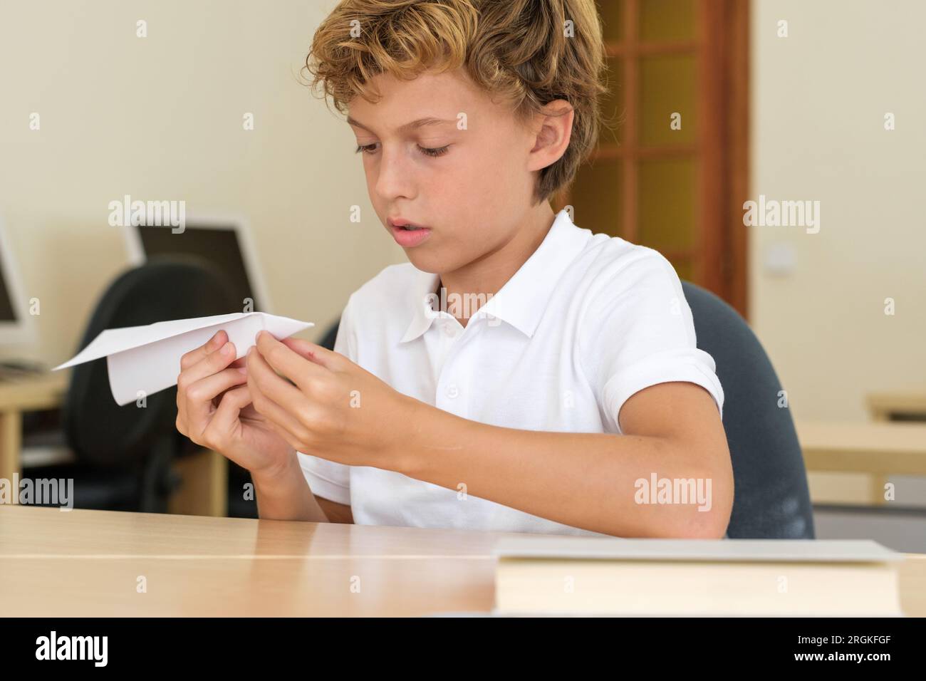 Concentrated schoolchild creating white paper plane while sitting at ...