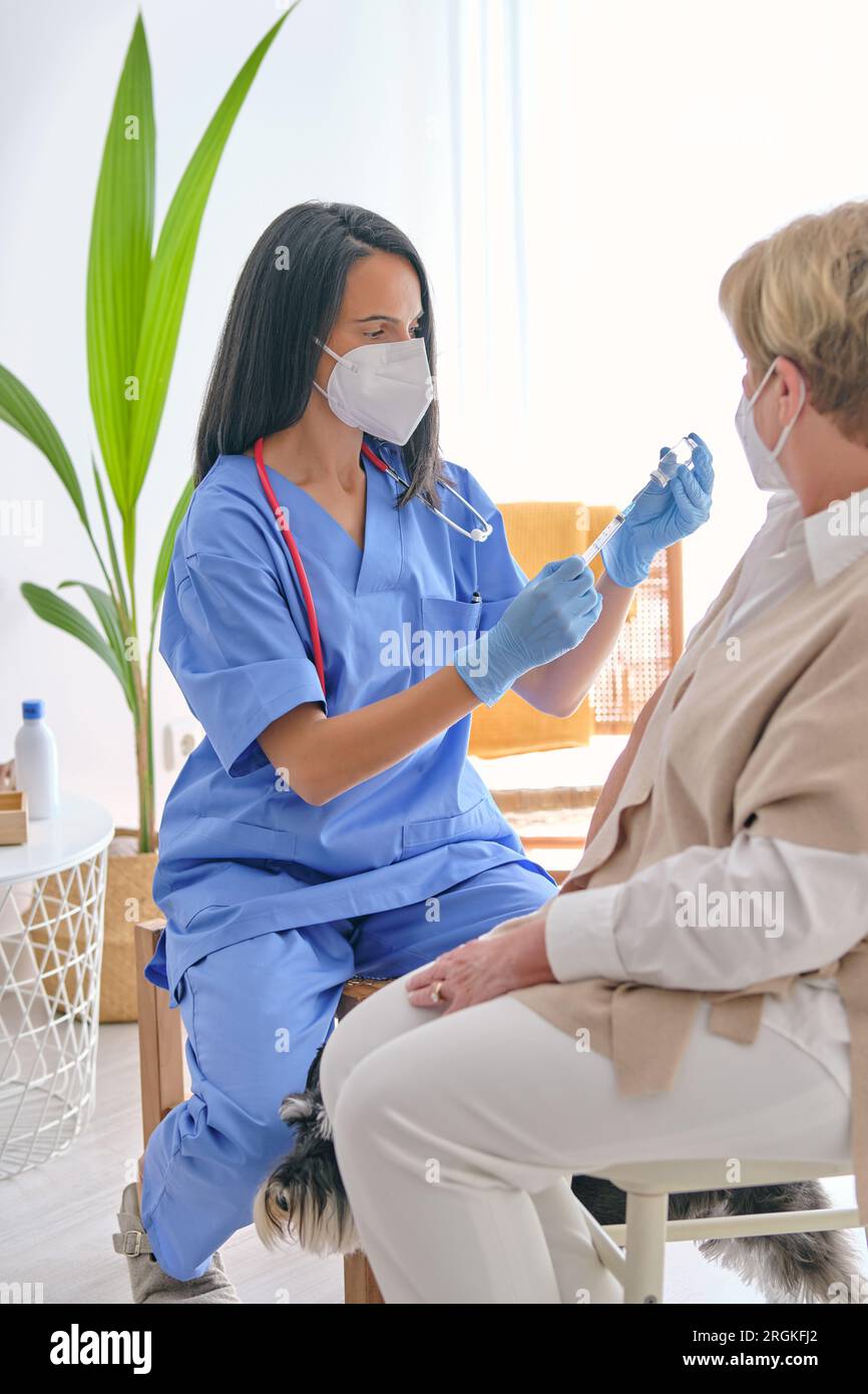 Female doctor in uniform and respiratory mask filling injector with ...