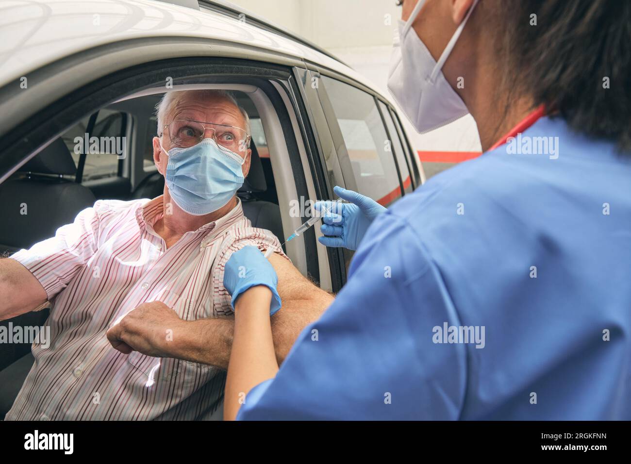 Crop anonymous nurse inoculating senior male driver in sterile mask ...