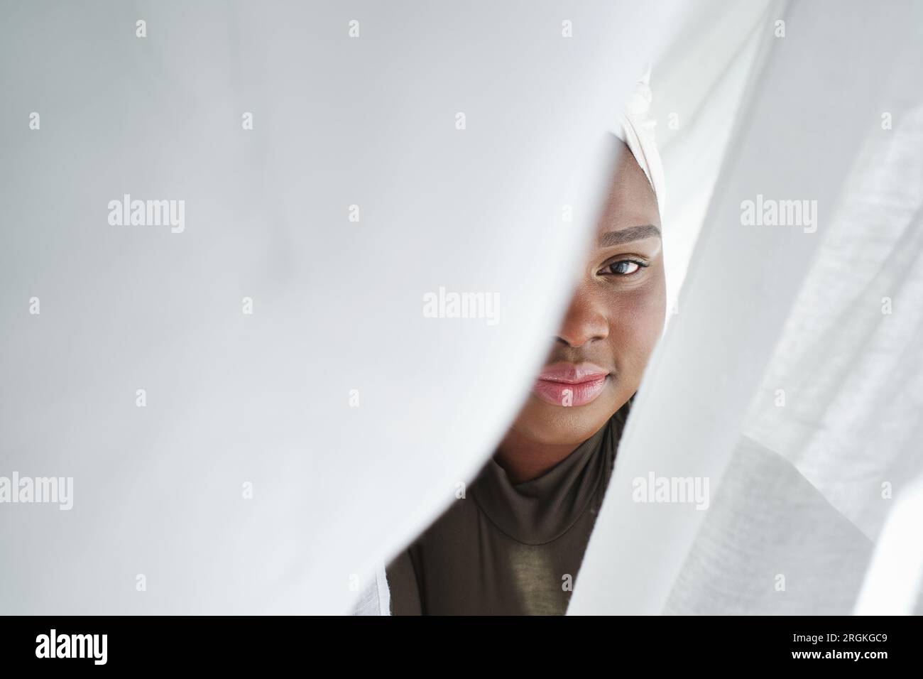 Beautiful black female model in turban looking at camera and hiding ...