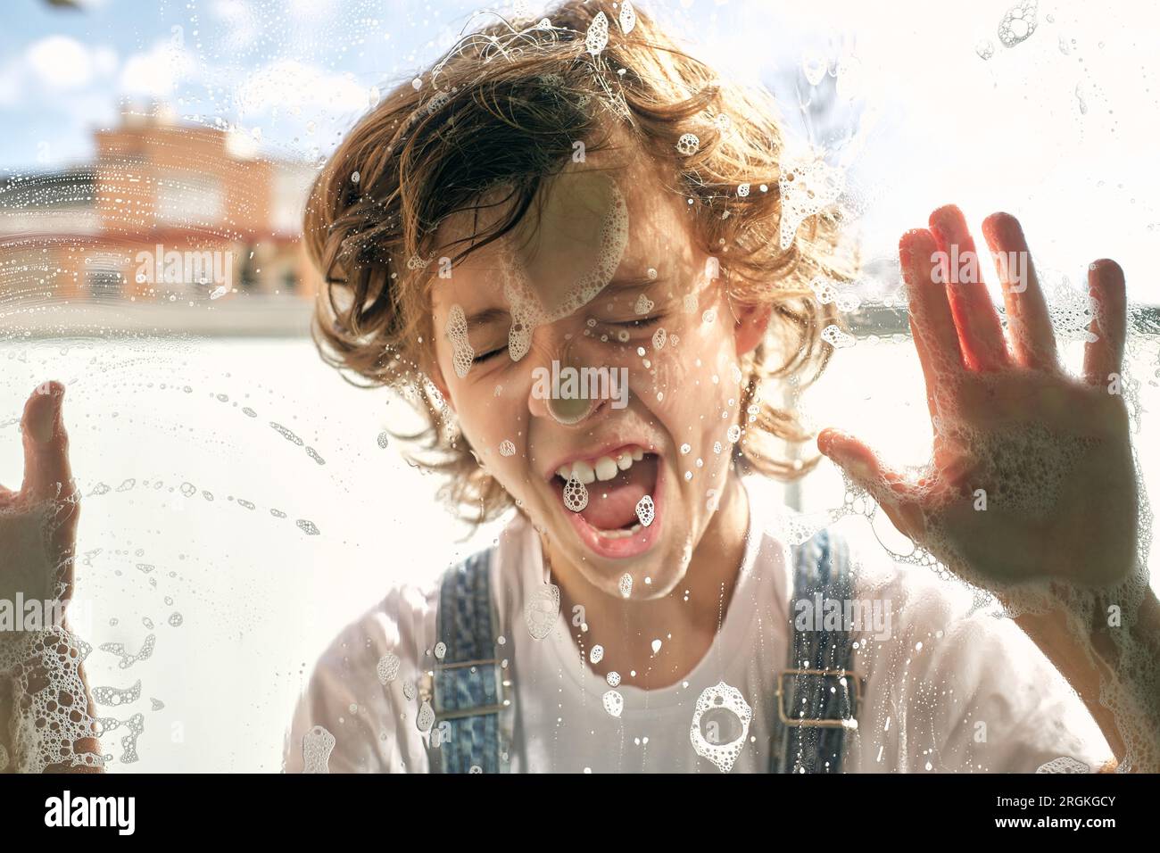Through glass of excited boy with eyes closed screaming while washing ...