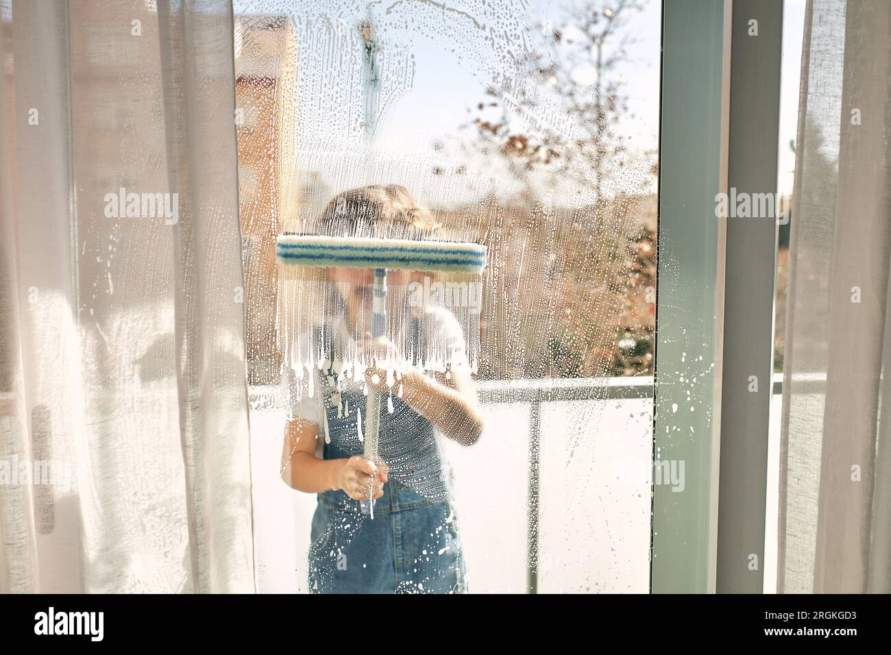 Through window of anonymous child in casual clothes doing household ...