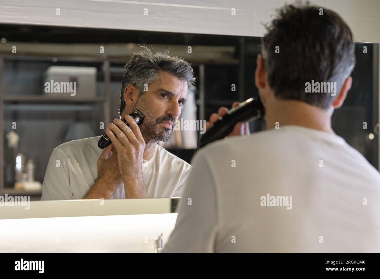 Concentrated male in casual clothes shaving beard using professional ...