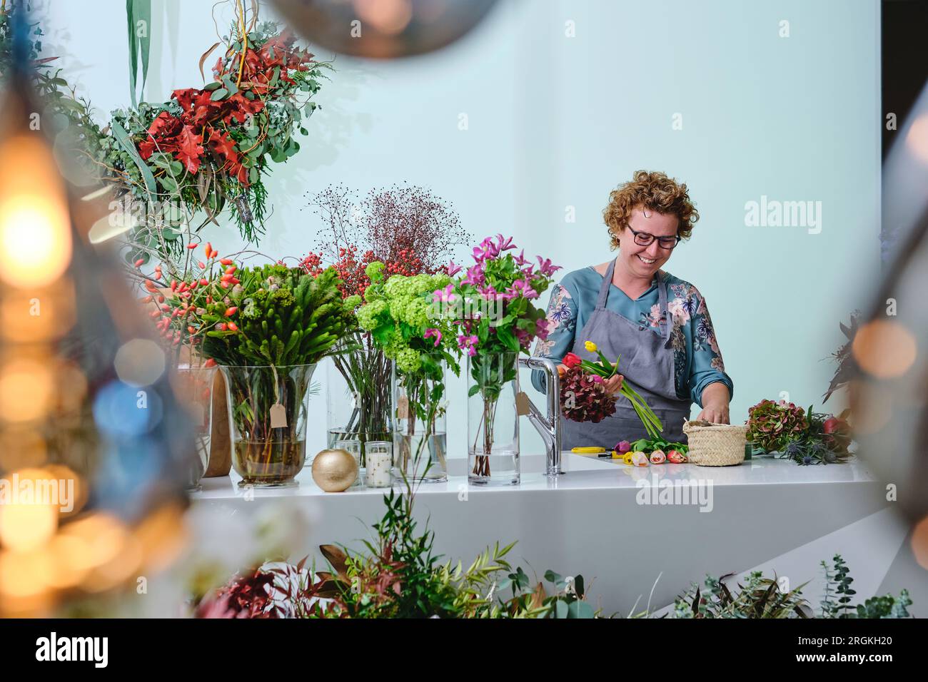 Smiling mature female florist with short curly hair in glasses and ...