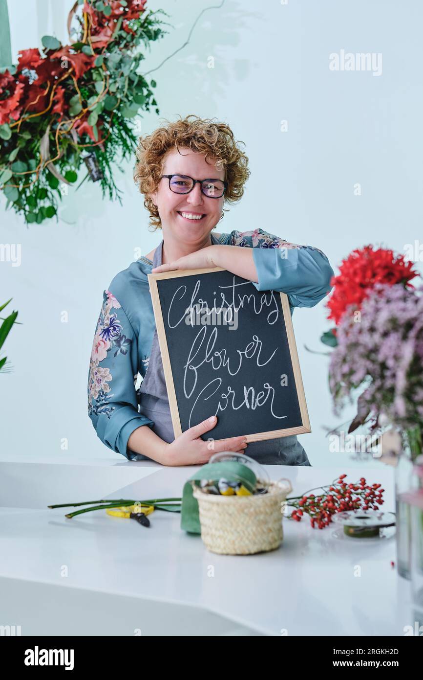 Professional female florist with curly hair smiling and looking at ...