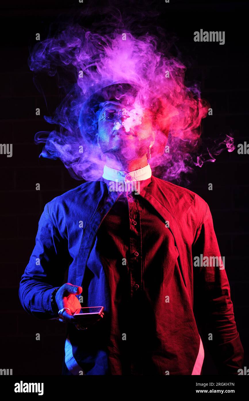 Black male with smartphone in hand vaping against black background in ...