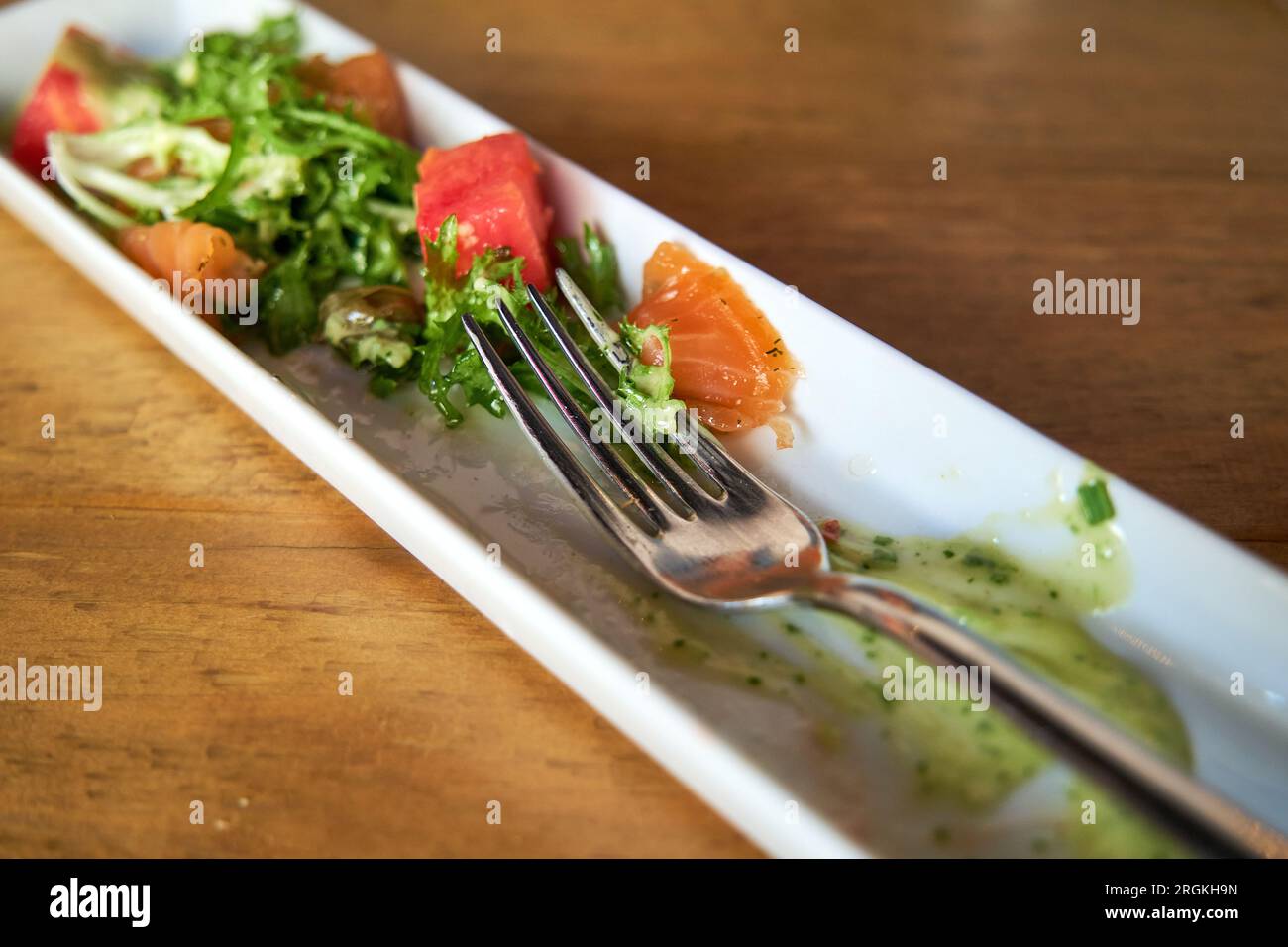 Fork in a rectangular white dish of marinated salmon with escarole ...