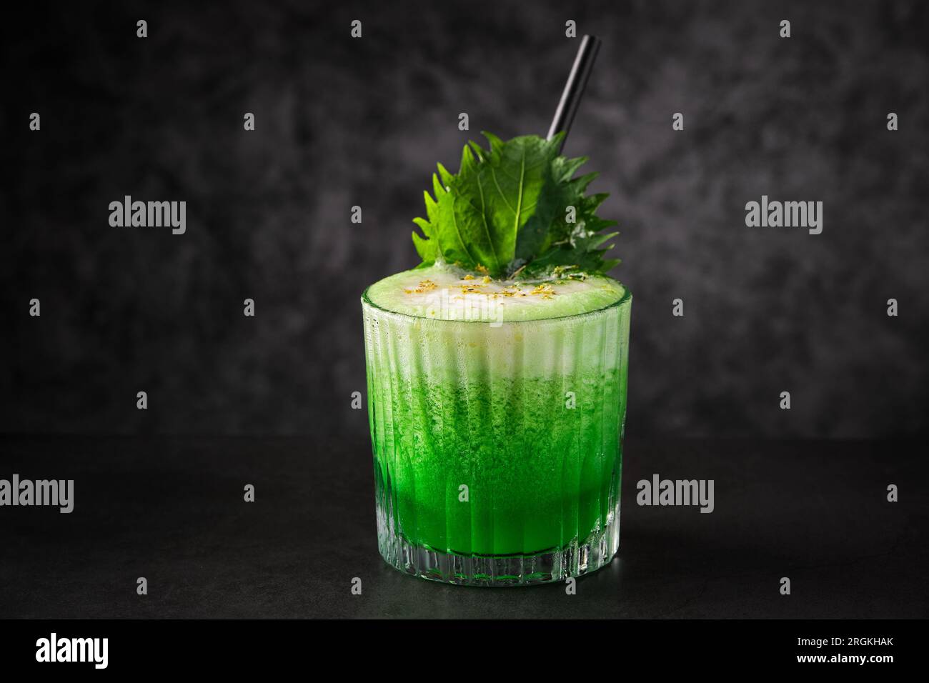 Glass of green alcohol cocktail with froth garnished with shiso leaf ...