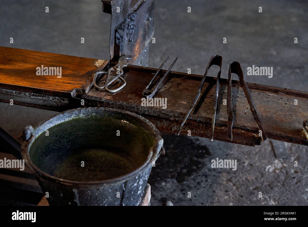 Various glassblowing old tools on wooden bench near bucket filled with ...