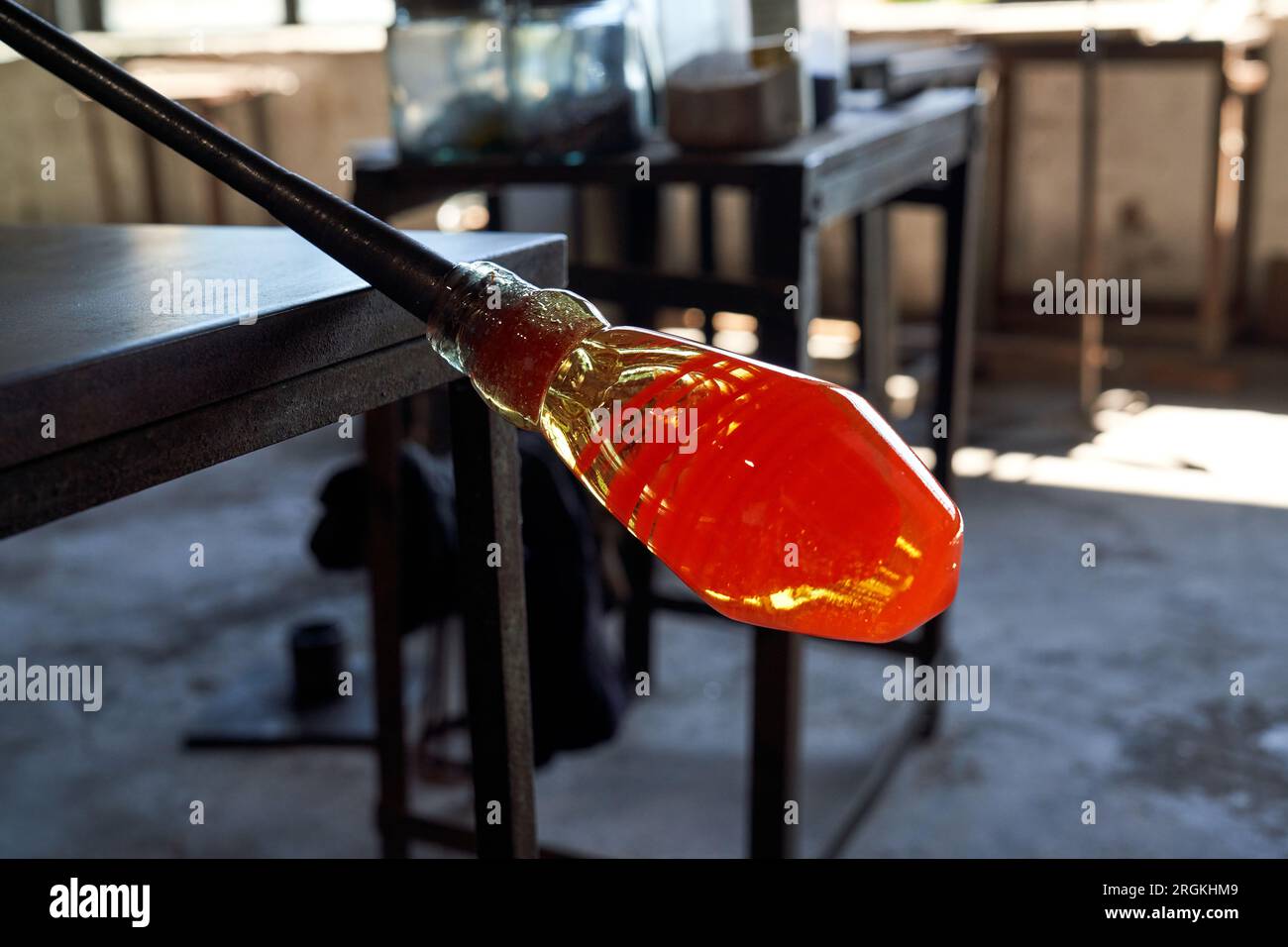 Heated liquid glass on tip of blowpipe in process of making hookah vase ...