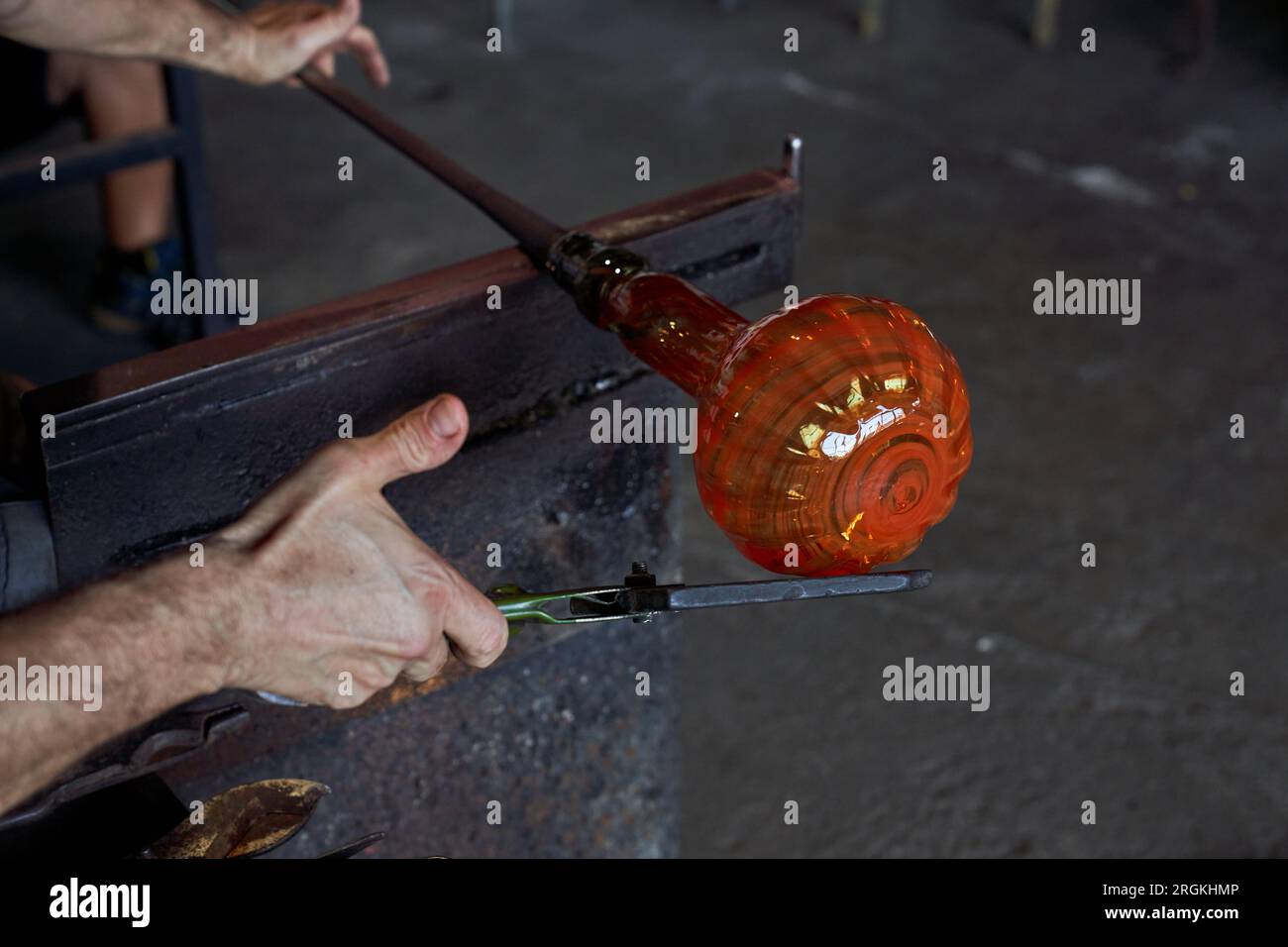 High angle of anonymous glassmith shaping hot glass with paddle while ...