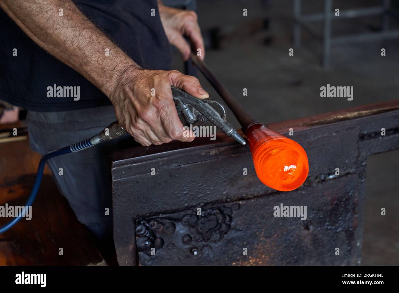 High angle of unrecognizable glassblower holding blow tube and blowing ...