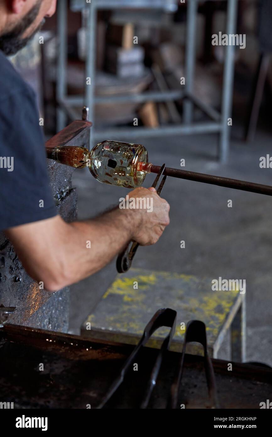 Anonymous male master with tool shaping hot glass on blowpipe in ...