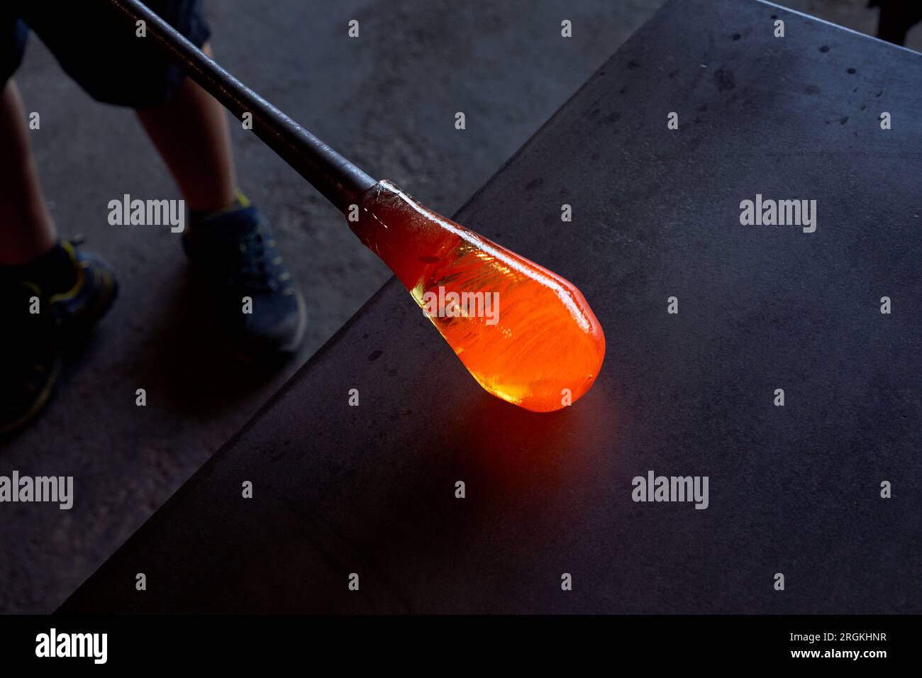 From above of anonymous glassmith putting blowpipe with hot melted ...