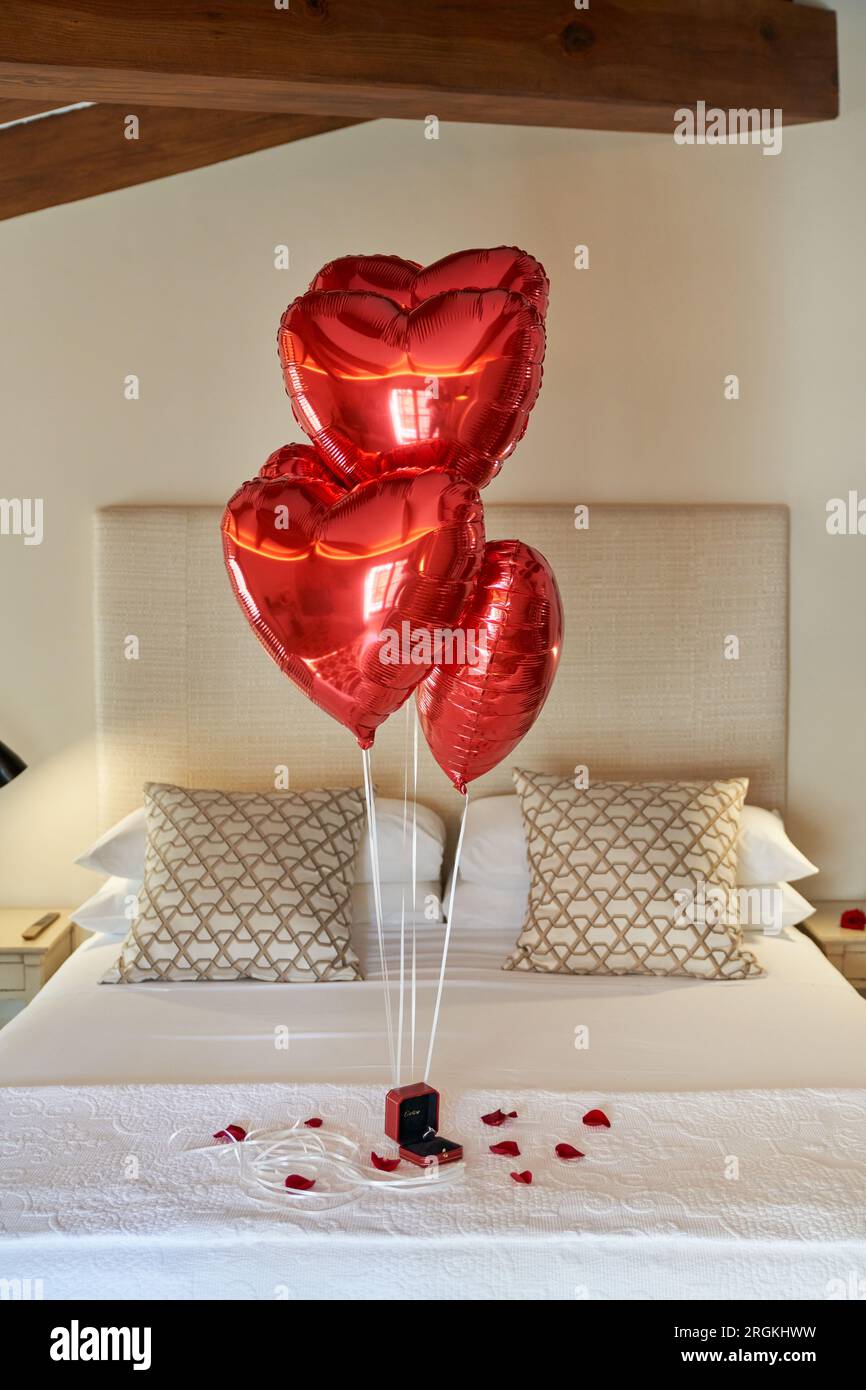 Hotel bedroom decorated with red heart shaped balloons and scattered ...