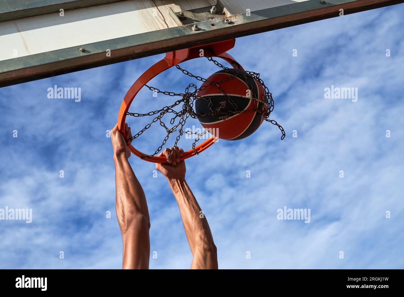 Low angle of unrecognizable black male player hanging on hoop while throwing ball into basket ...