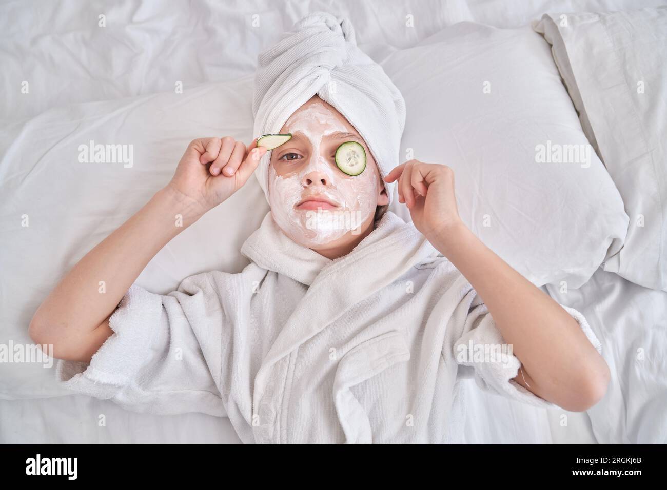 Top view of serious child in towel turban and bathrobe putting off ...