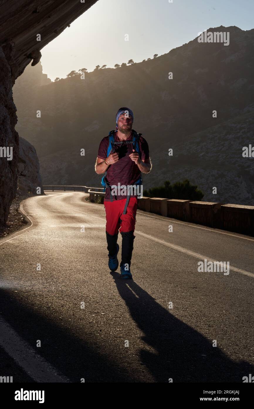 Full body of bearded male hiker in bandana walking on asphalt roadway ...
