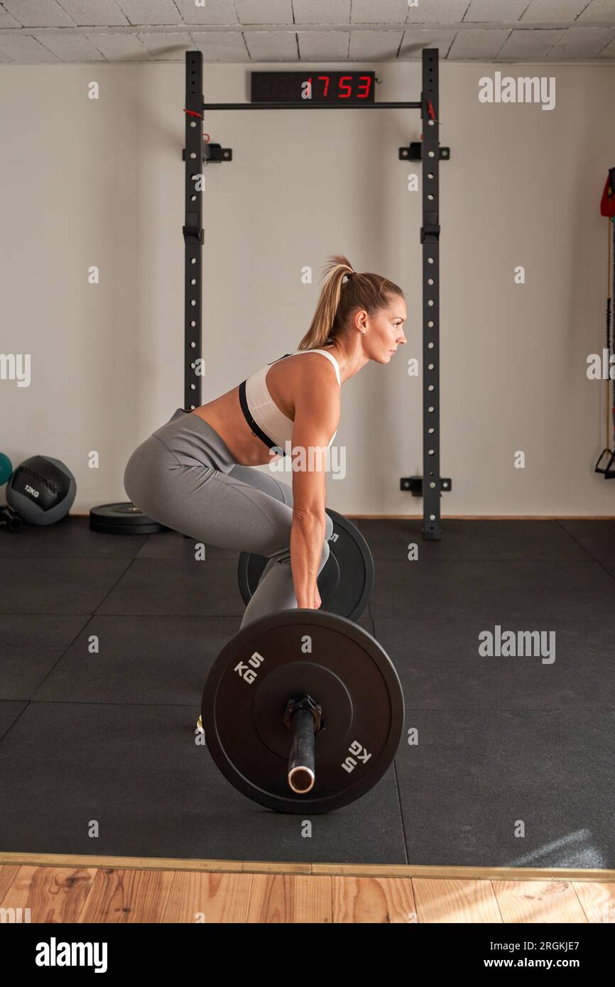 Side view of strong female athlete in sportswear doing deadlift ...