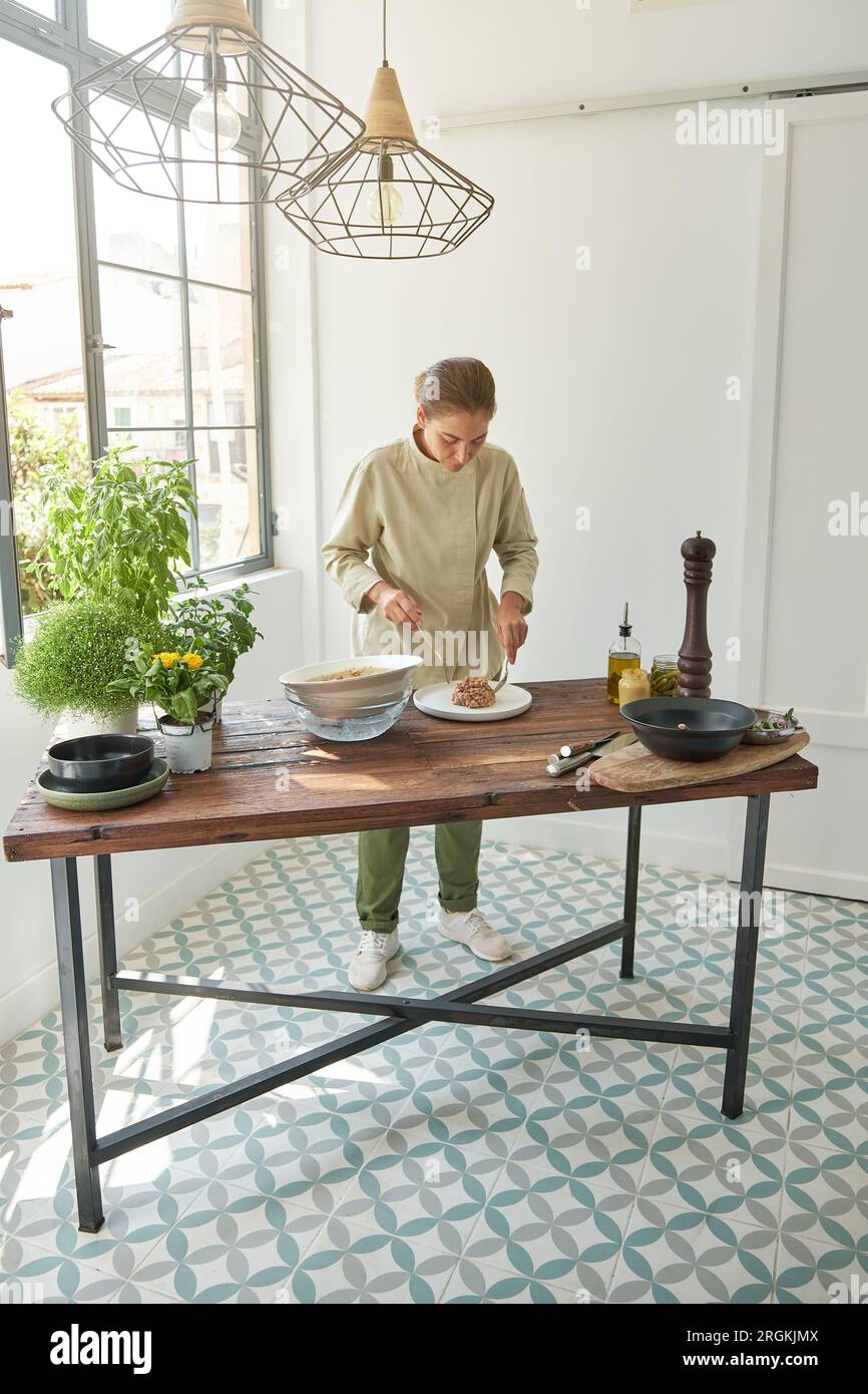 Full body of concentrated female cook in uniform putting steak tartare ...