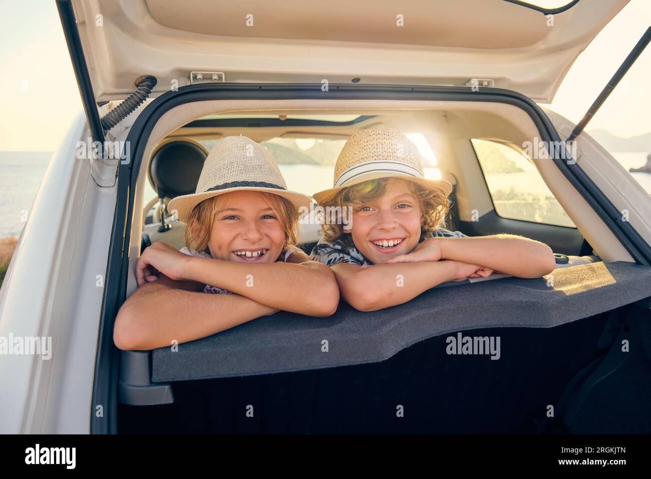 Two children in straw hats leaning in the back seats of a car sticking ...