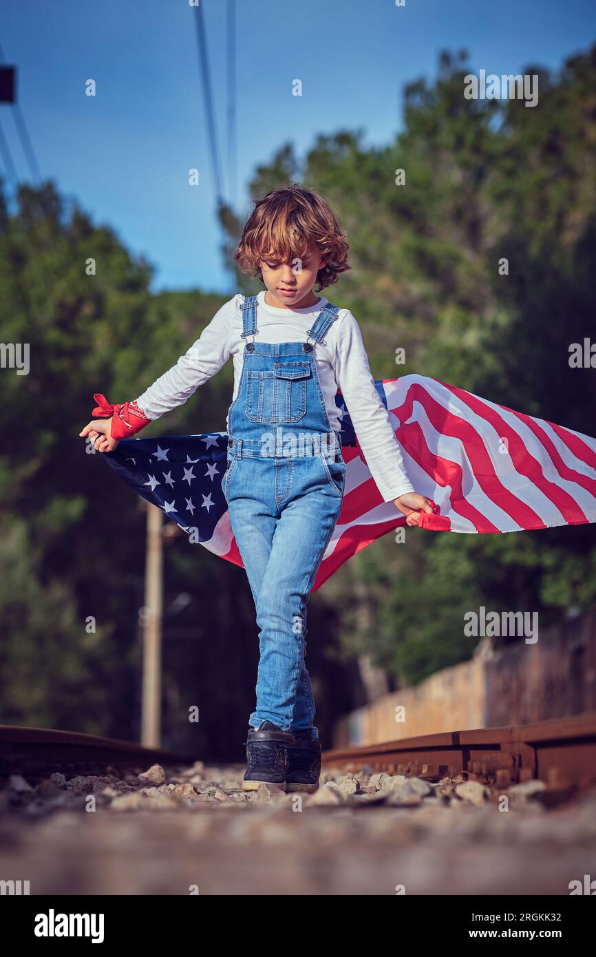 Boy in jeans overall looking down while walking on crushed stones ...