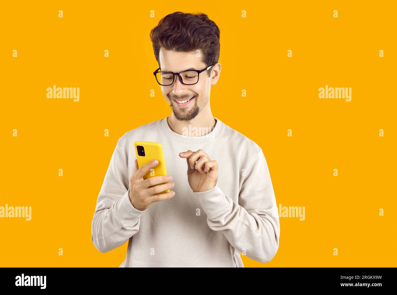 Cute smiling guy with glasses looks at the screen of his smartphone and ...