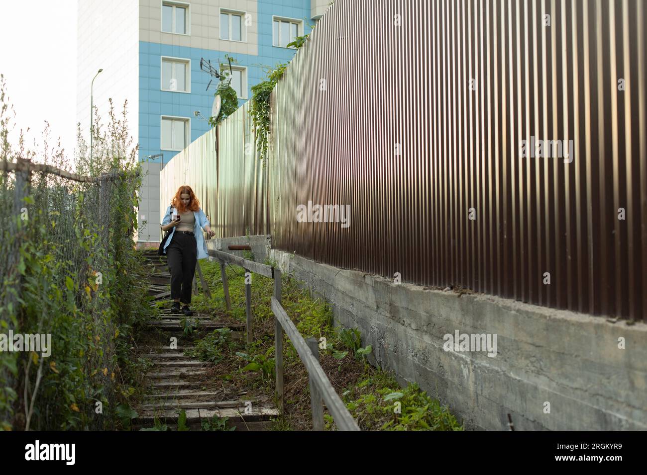 Girl walks up old staircase. Passage between fences. Village and town ...