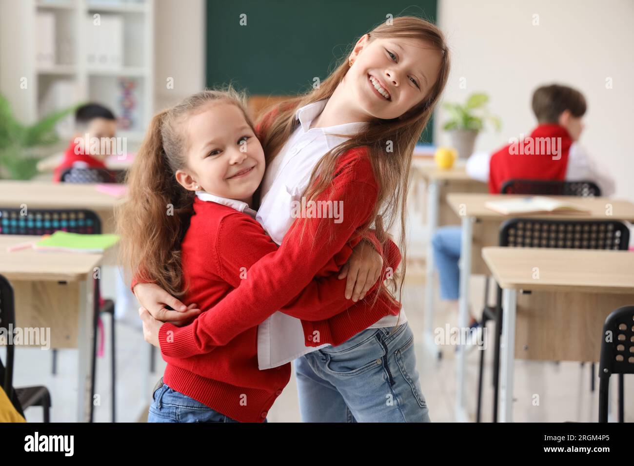 Happy little girls hugging in classroom Stock Photo - Alamy