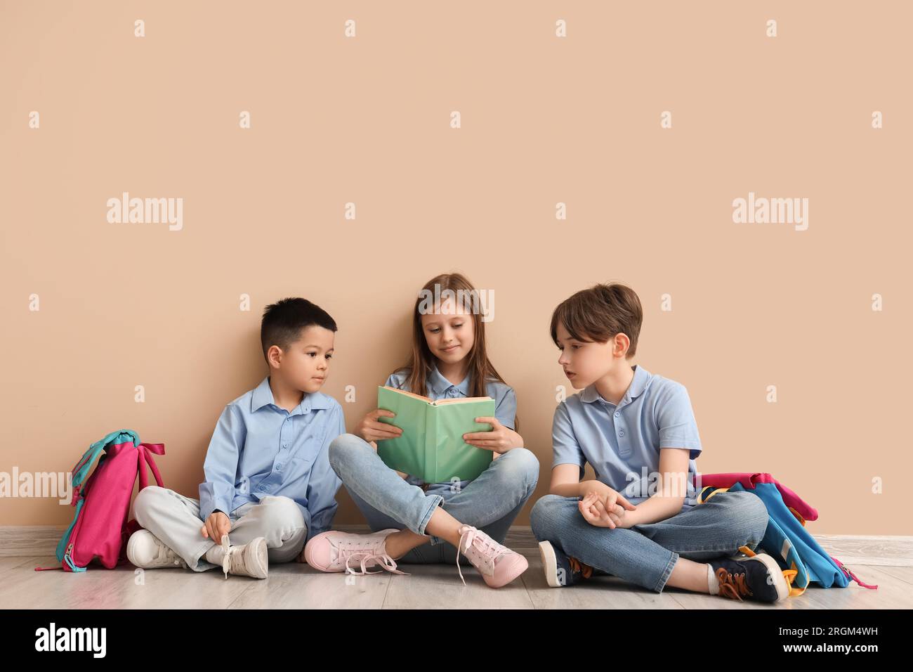Little pupils reading book near beige wall Stock Photo - Alamy