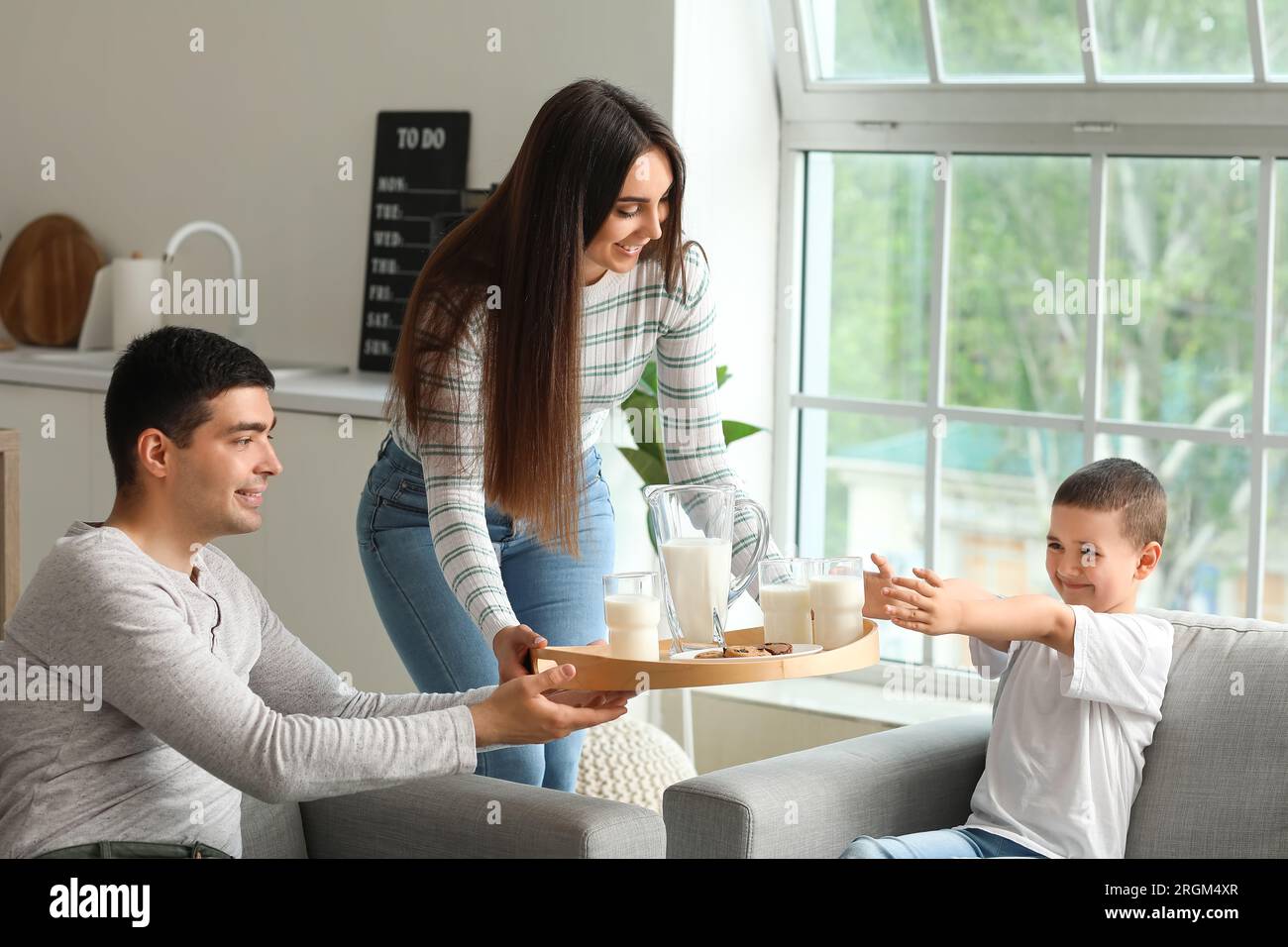 Young woman bringing tray with milk and cookies to her family at home ...
