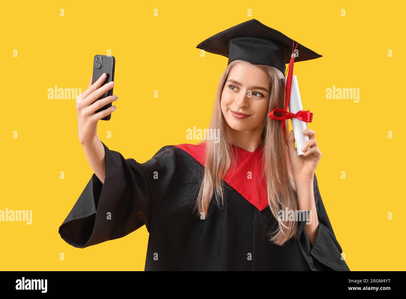 Female graduate student with diploma taking selfie on yellow background ...