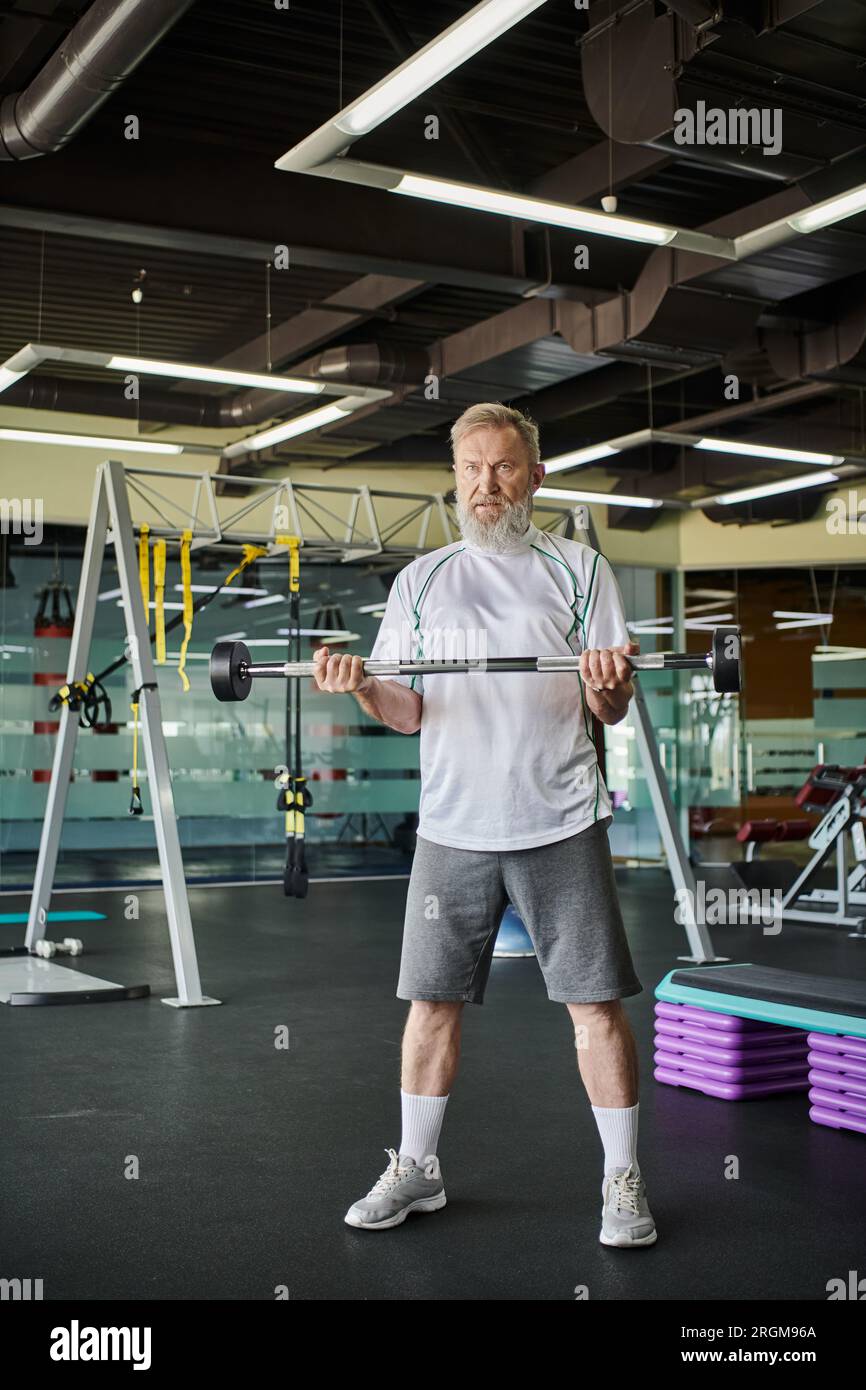 athletic elderly man with beard working out with barbell in gym, active ...