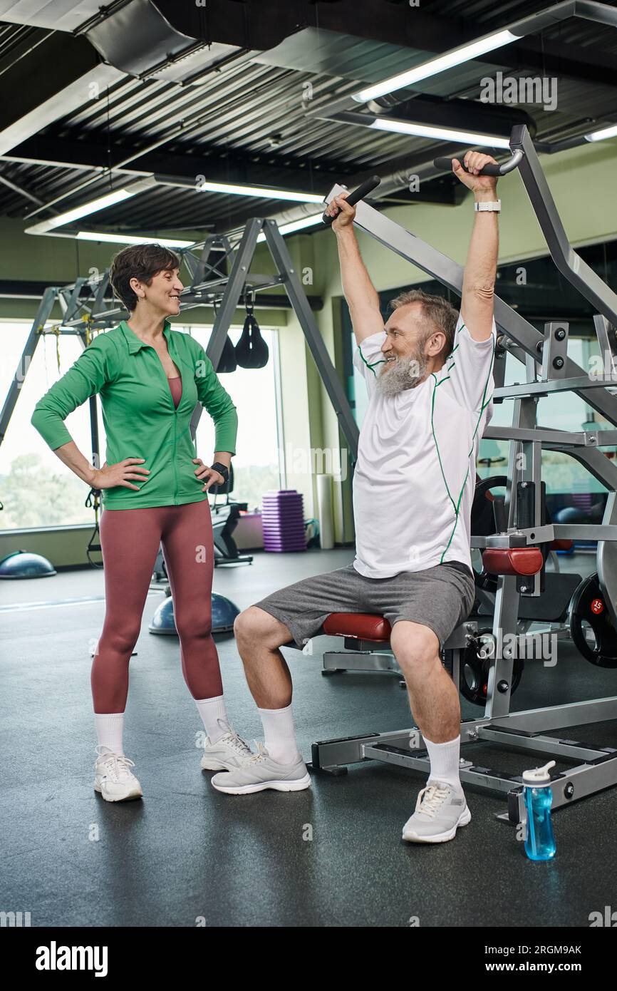 strong and elderly man with beard working out on exercise machine near ...
