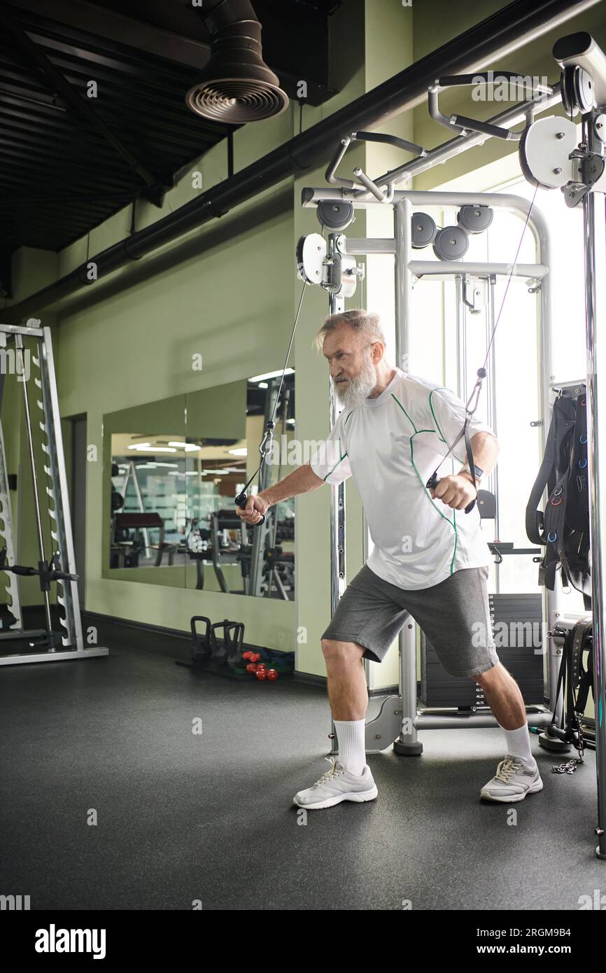 concentrated elderly man with beard working out on exercise machine in ...