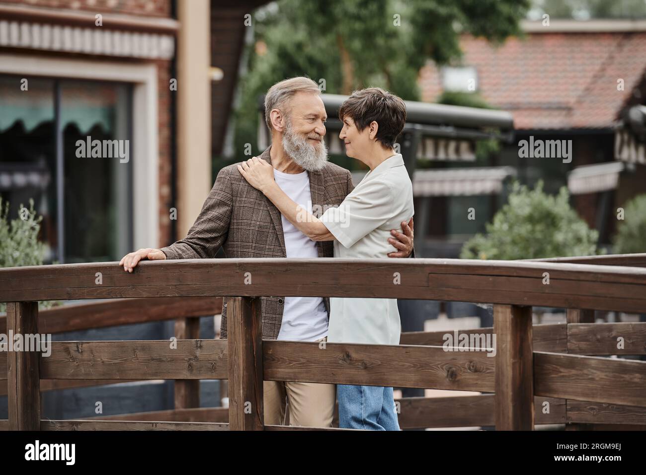 romantic senior couple standing together on wooden bridge and hugging each other, elderly love ...