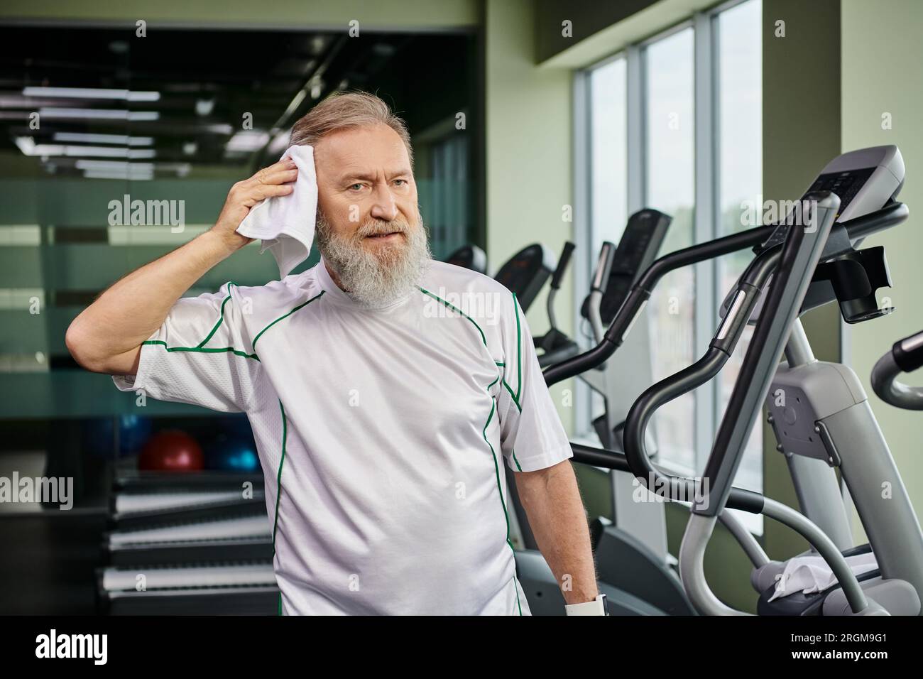 elderly man with beard wiping sweat with towel after working out in gym ...