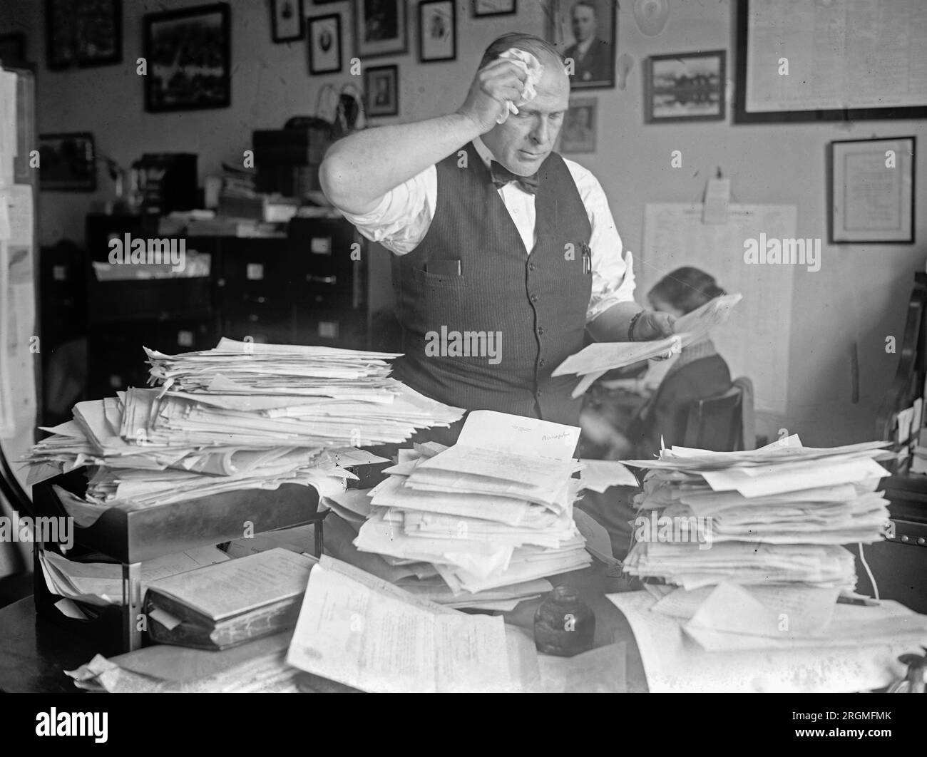 Roy G. Fitzgerald standing behind a very messy desk, wiping his ...
